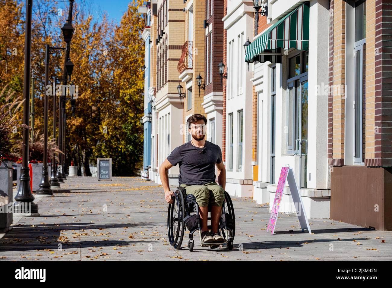 Young paraplegic man in his wheelchair going down a city walkway on a ...