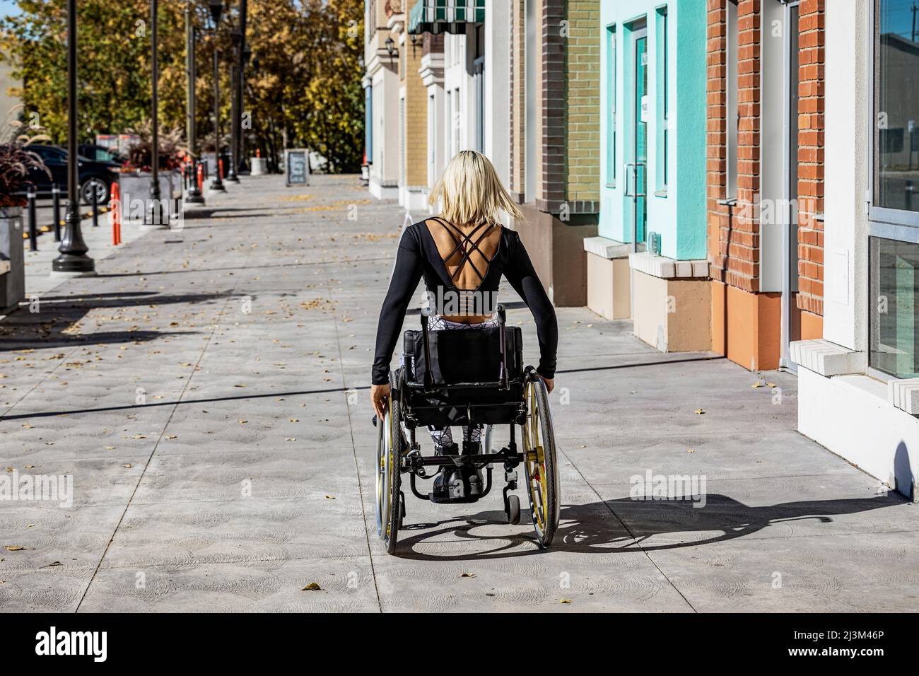 Young paraplegic woman in her wheelchair going down a city walkway on a ...