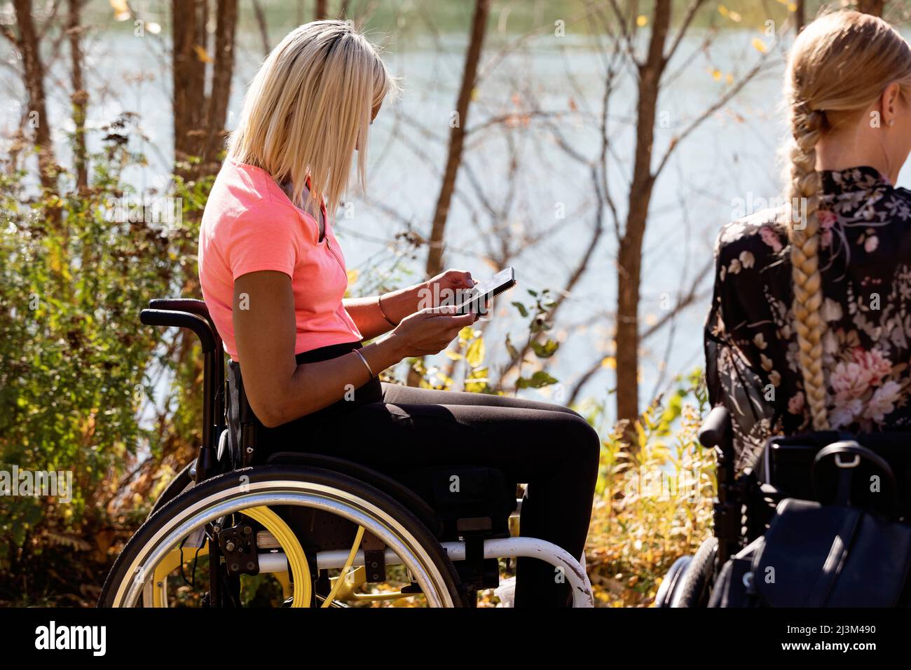 Paraplegic young woman using her smart phone while friends enjoy a ...