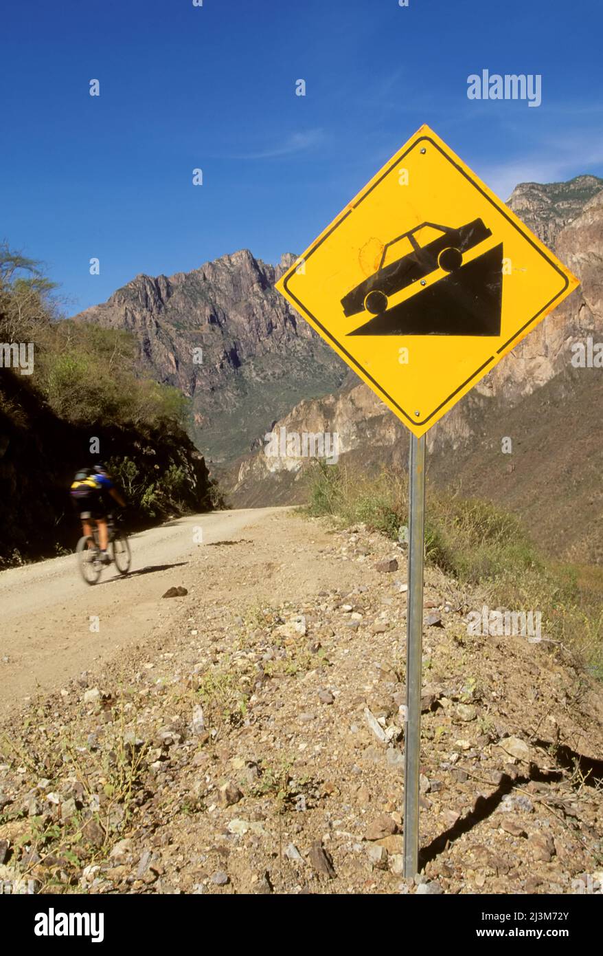 A biker heads downhill past a steep slope sign.; Batopillas Canyon ...