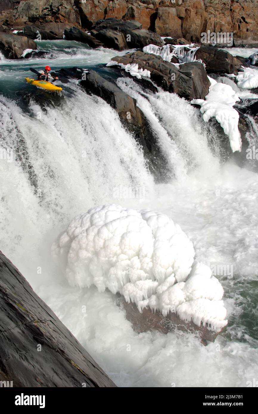 A winter whitewater kayaker on the verge of a big waterfall and ice ...