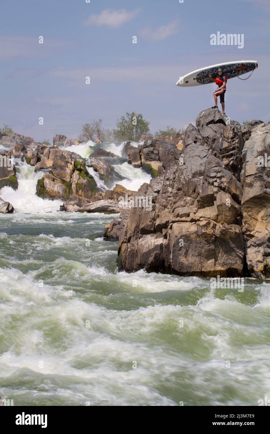 A stand up paddle boarder poses on rocks below Great Falls.; Potomac ...