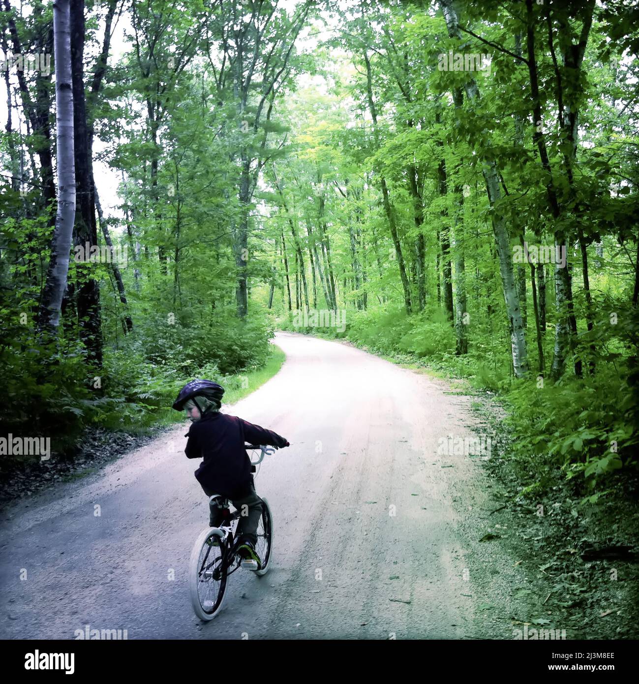 An eight year old boy rides his bike down a forest lane near Sebago Lake, Maine.; Sebago Lake ...
