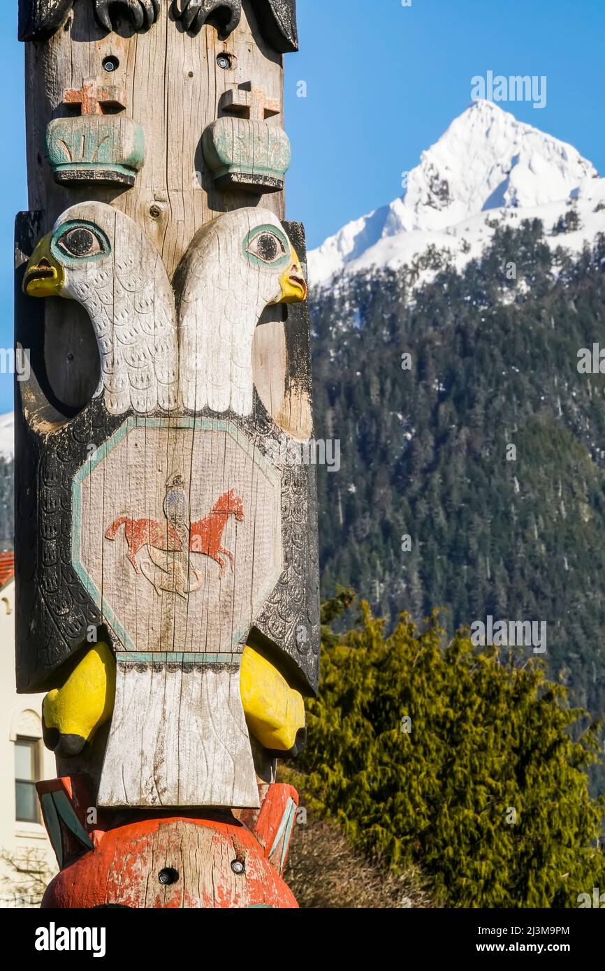 Close-up detail of a totem pole and the forested mountainside with snow ...