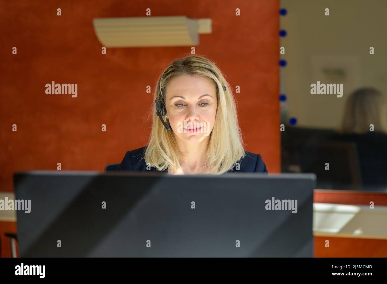 Smiling businesswoman wearing a headset working at a computer looking ...