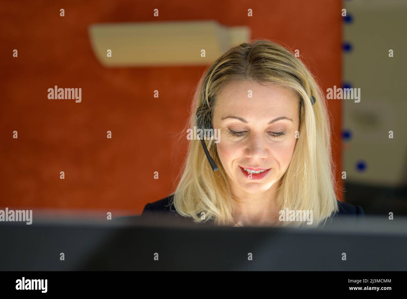 Smiling businesswoman wearing a headset working at a computer looking ...