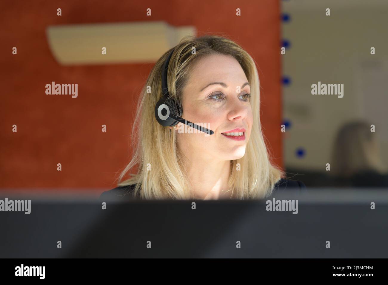 Receptionist or call centre operator taking a telephone call on a headset viewed over the top of ...