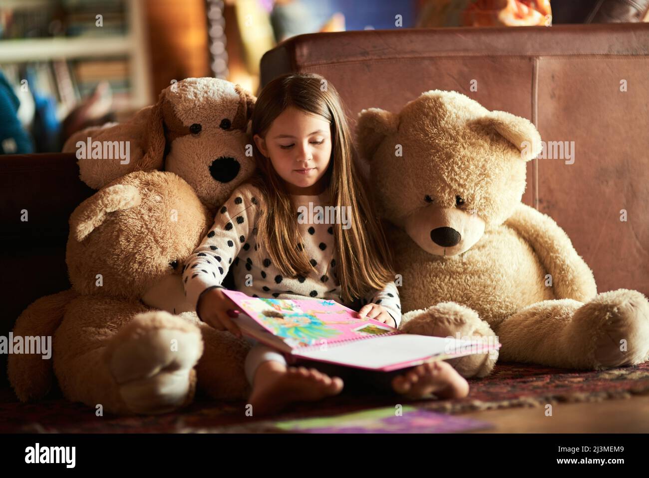 Reading her teddies a story. Shot of a little girl reading a book with ...