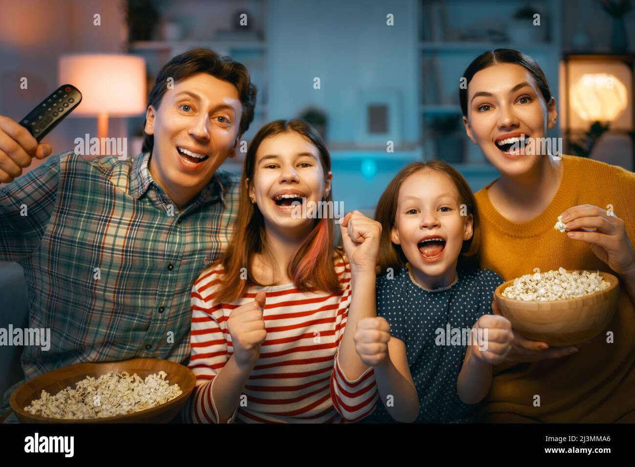 Happy family watching projector, TV, movies with popcorn in the evening ...