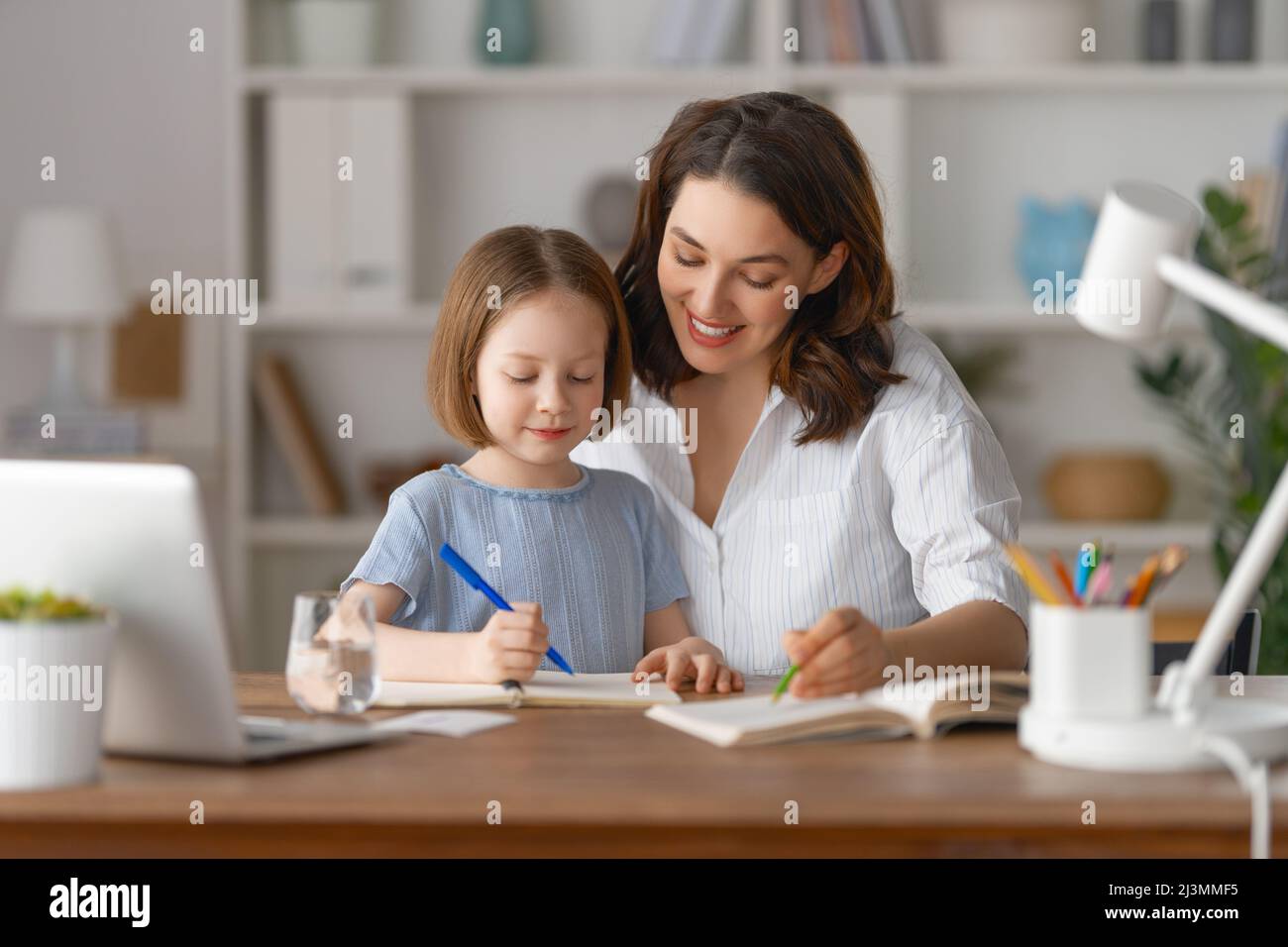 Happy child and adult are sitting at desk. Girl doing homework or ...