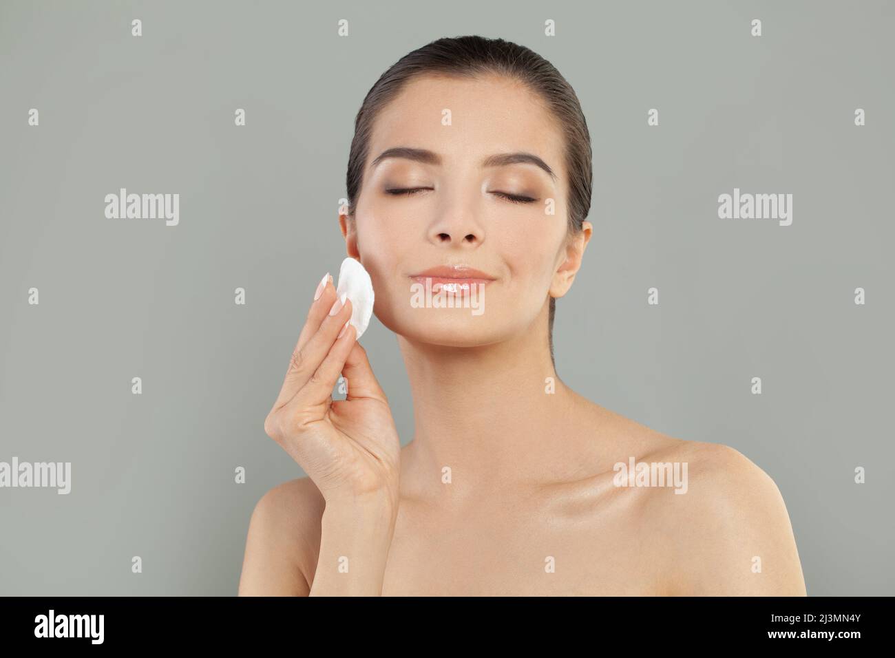 Young attractive woman cleaning her face with a cotton pad and smiling ...