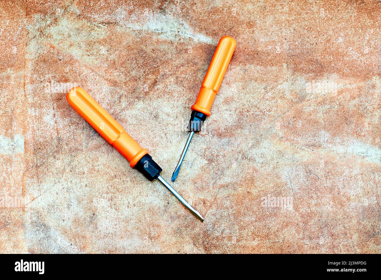 Two orange screwdrivers on brown marble tiles Stock Photo - Alamy