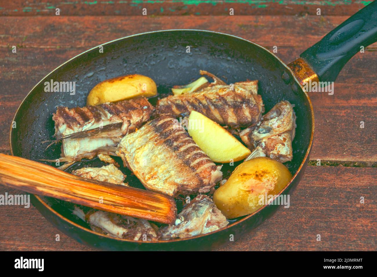 Field food. Fried fish and jacket potato in a frying pan with a ...