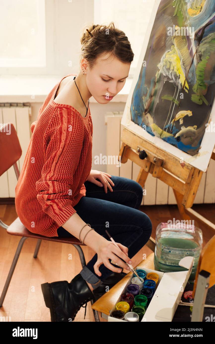 Beautiful woman artist drawing her picture on canvas with oil colors in ...