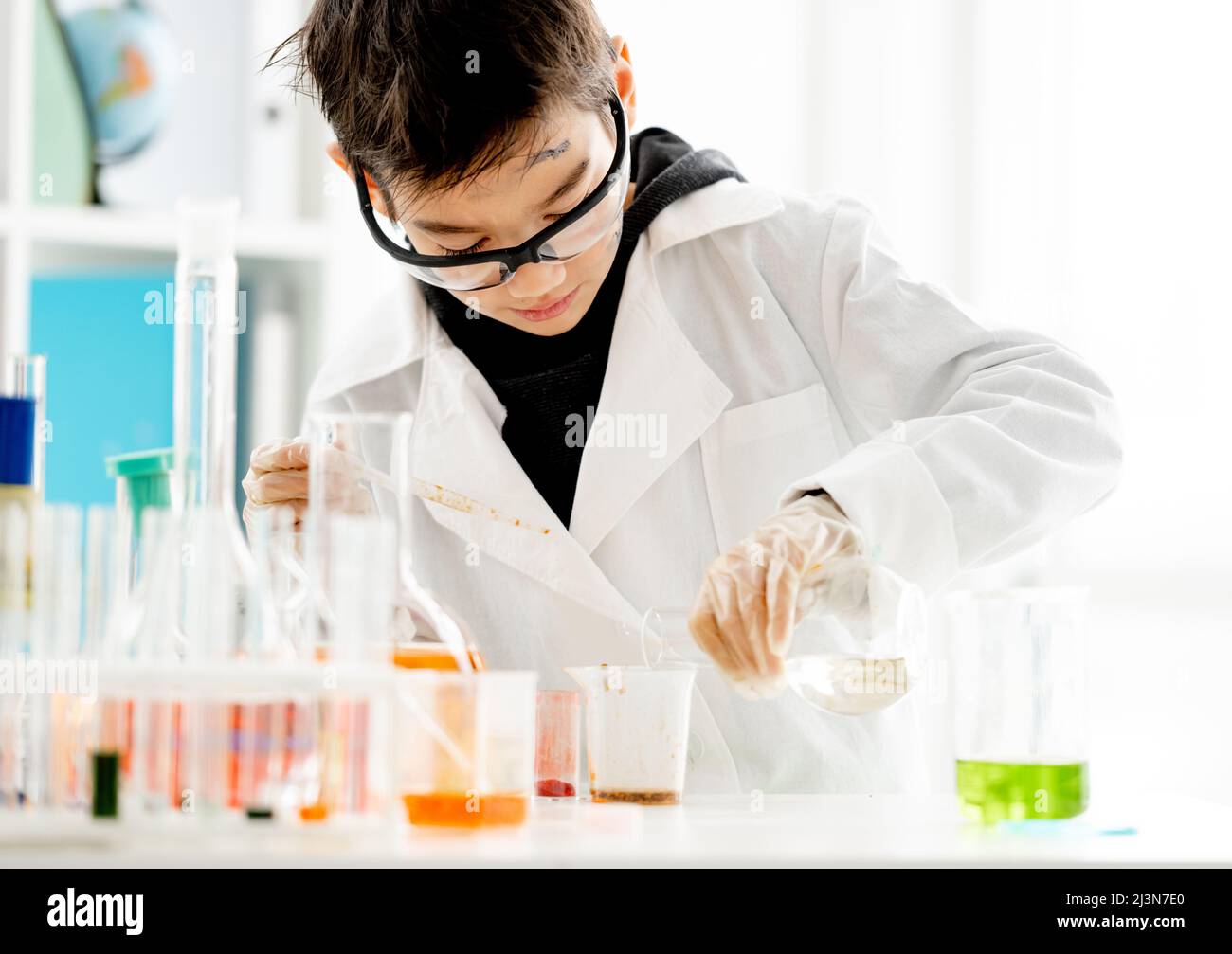 School boy wearing protection glasses with dirty face doing chemistry ...