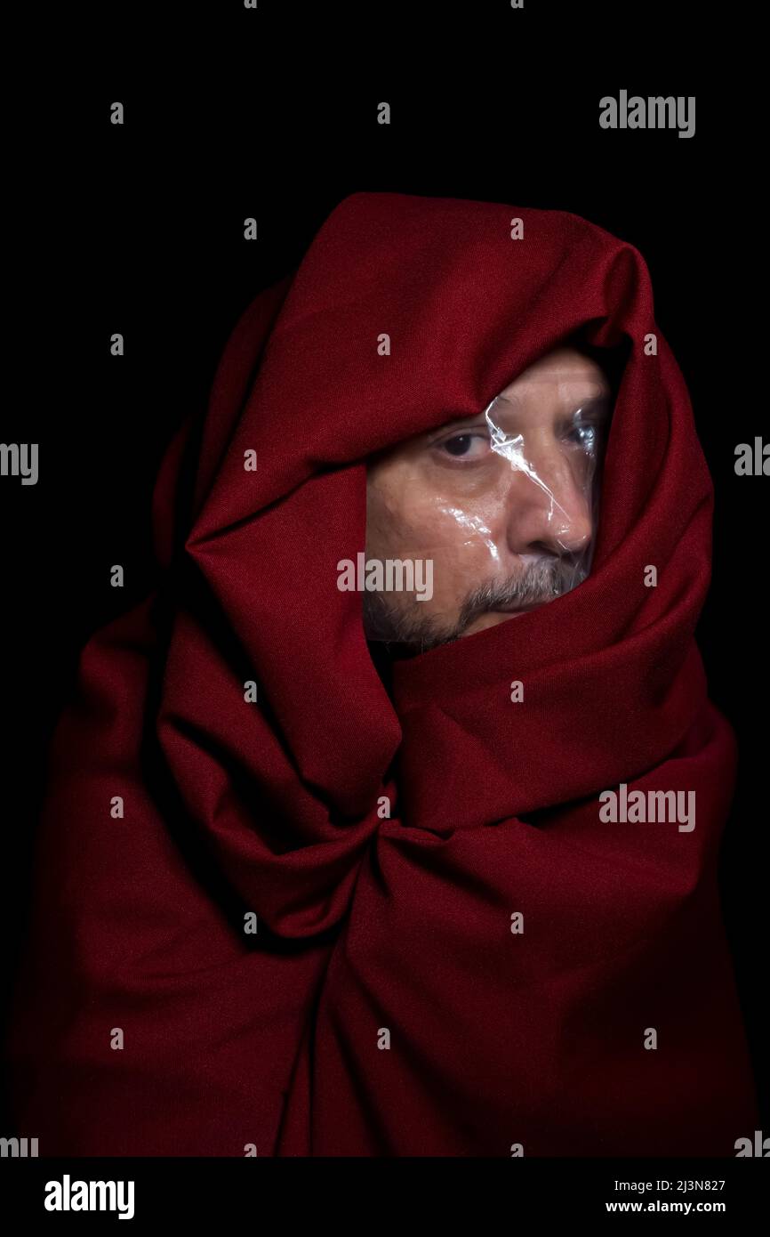 Man covered in red cloth with plastic on his face against black ...