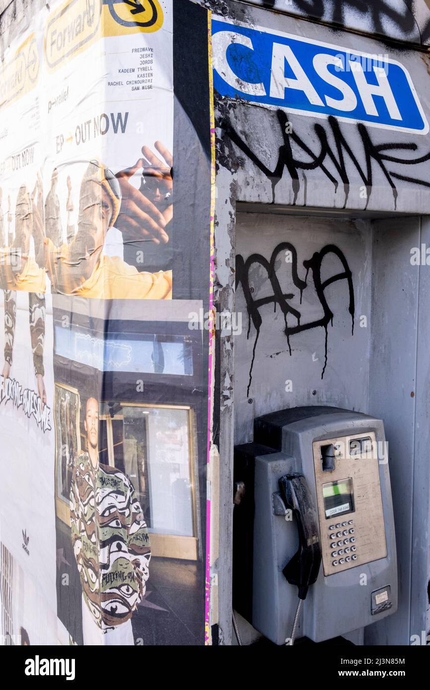 A cash dispenser and landline phone are covered in posters and graffiti ...