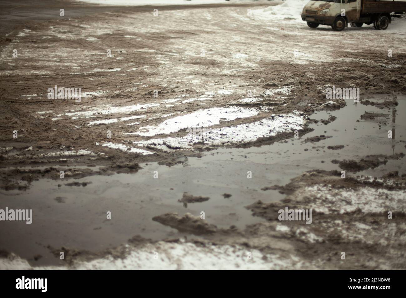Muddy puddle of melted snow on road. Uncleaned parking. Asphalt is ...