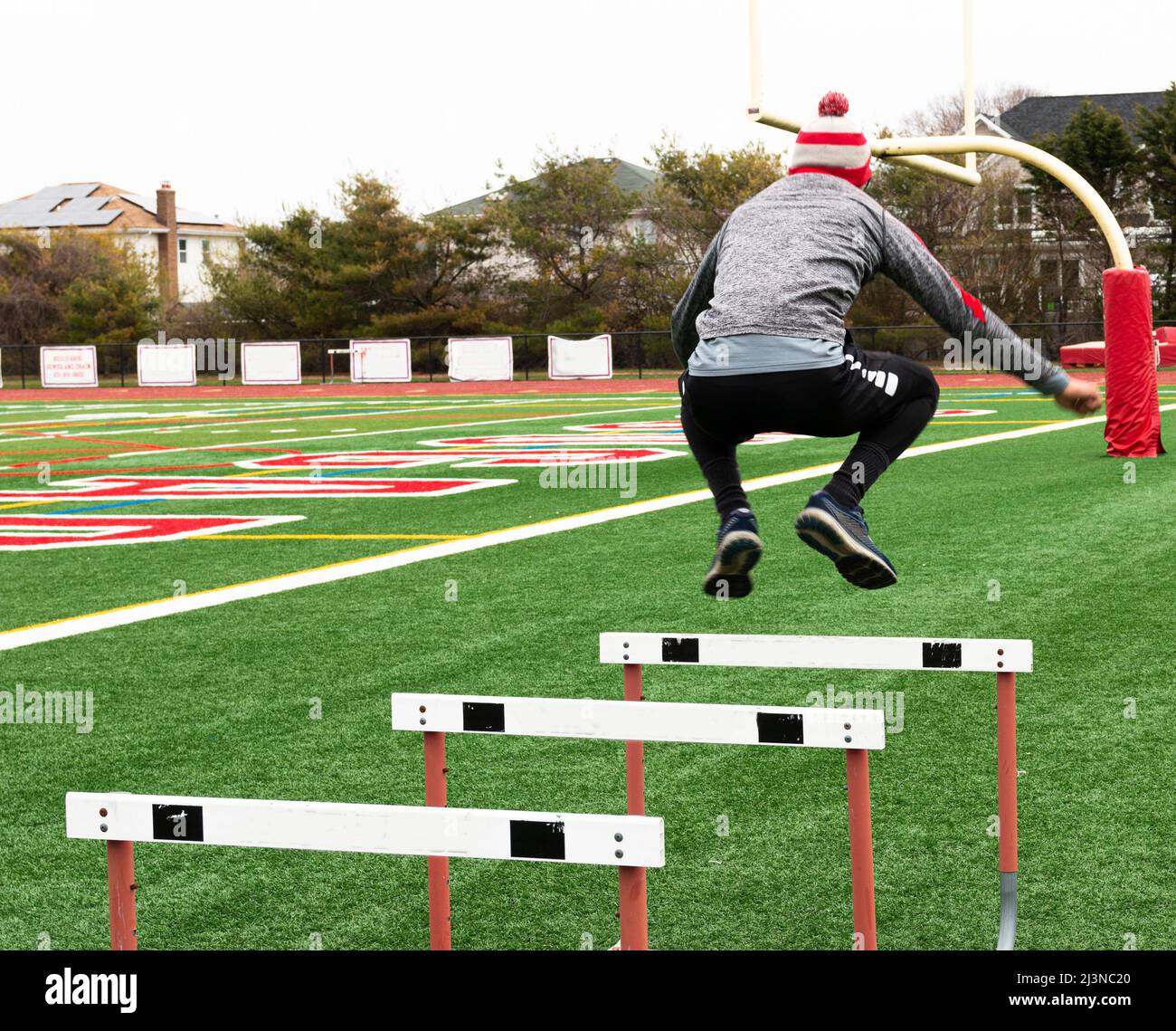 A High school boy finishing jumping over a few track hurdles at ...