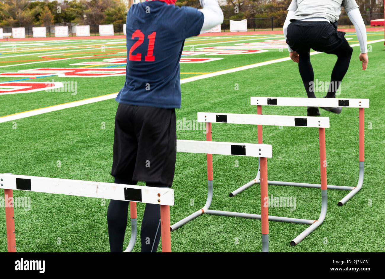 Rear view of two high school boys jumping over track hurdles on a green ...