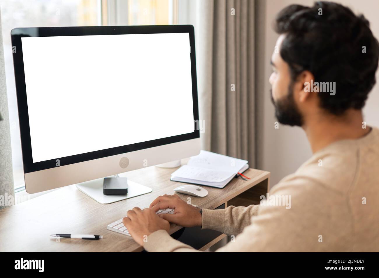 Back view of positive Hindi man in smart casual clothes using computer ...