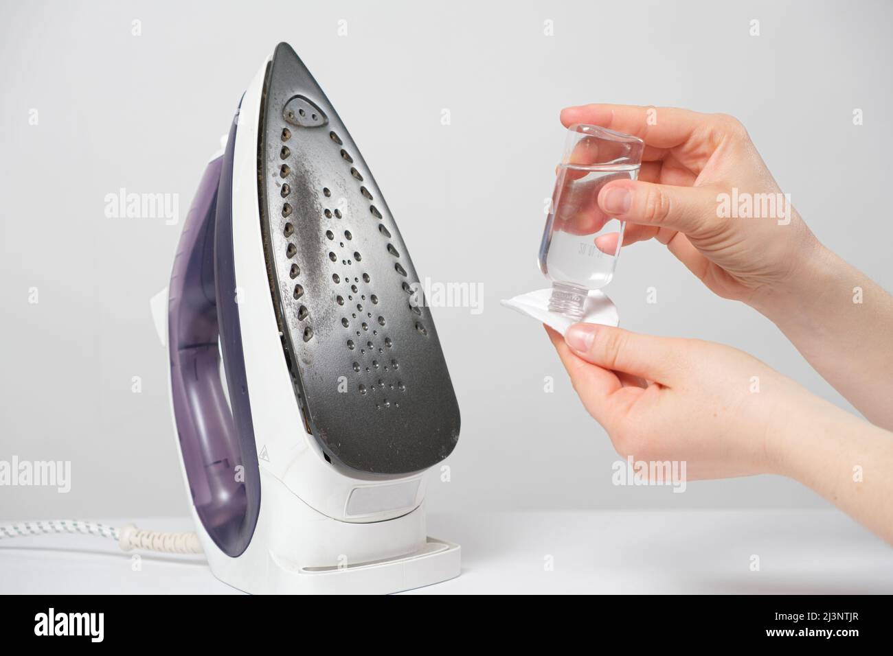 A woman cleans the sole of the iron from soot and scale with a special ...