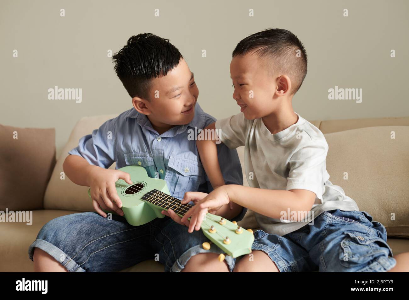 Cheerful preteen boy asking brother to let him play ukulele Stock Photo ...