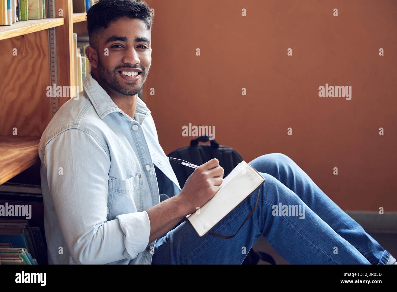 Revision done right. Shot of a young man making notes in a library at ...