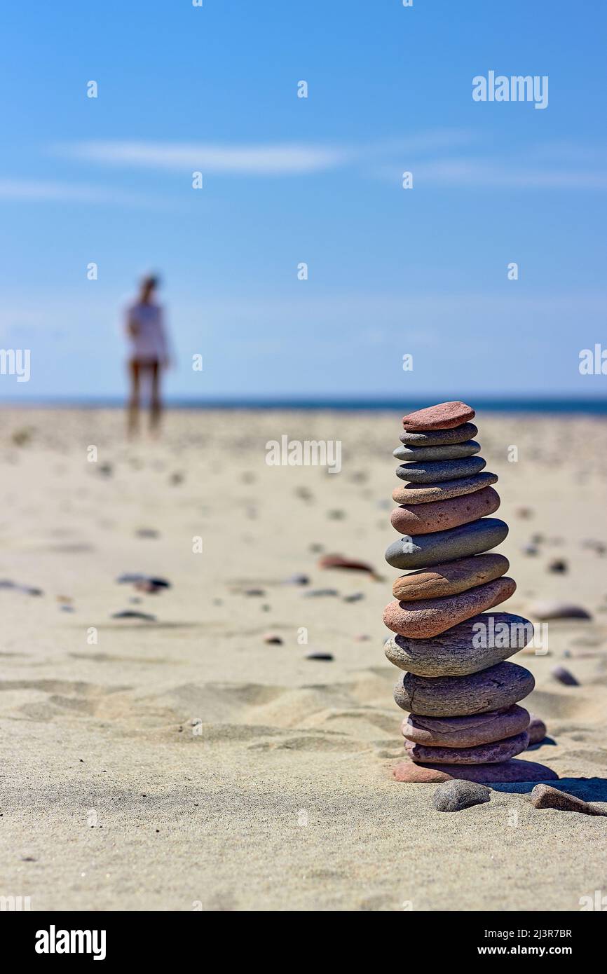Zen pyramid of balancing stones on a sandy beach with a woman walking ...