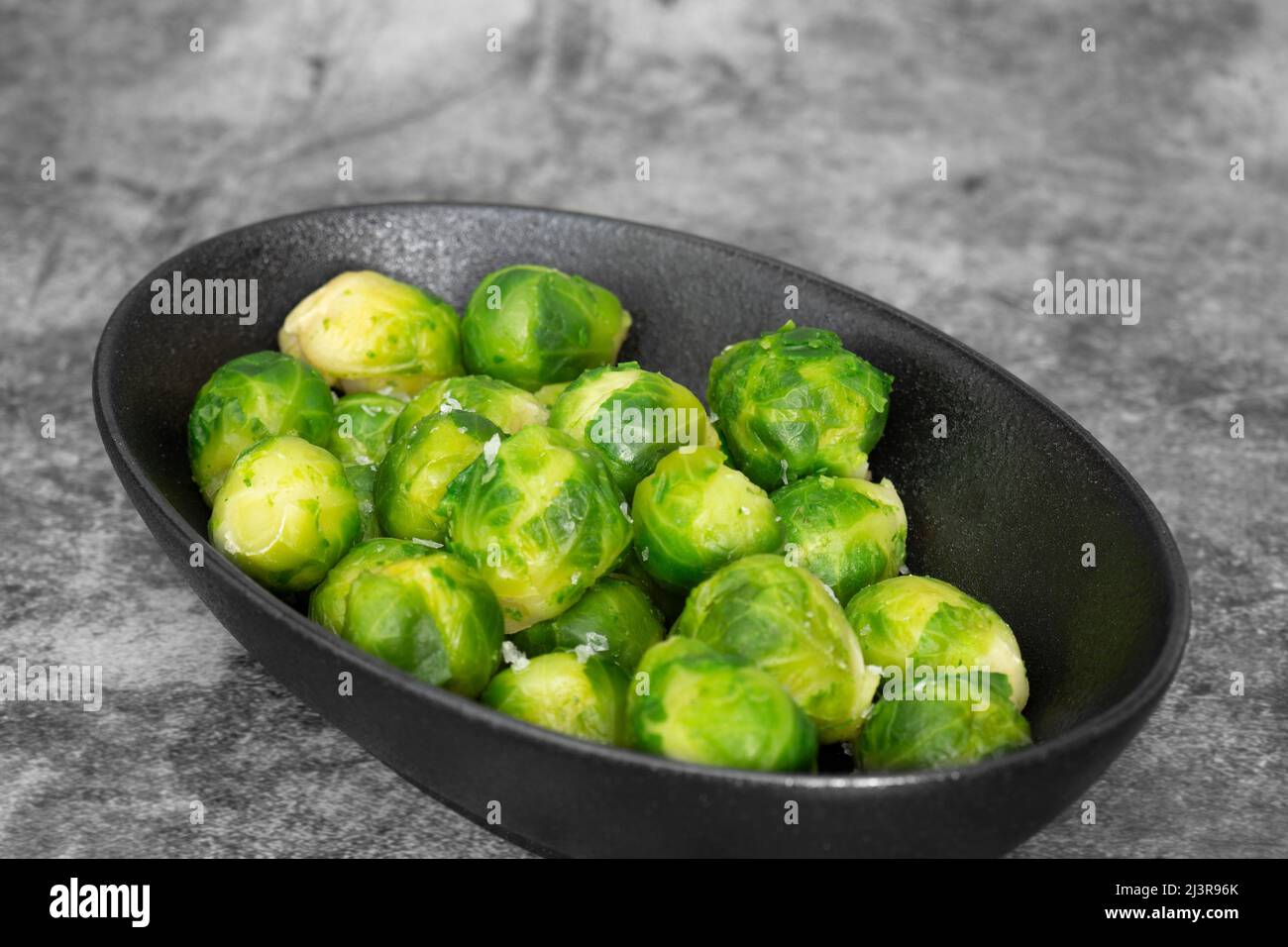 Brussels sprouts seasoned with sea salt in a black dish. On a stone ...