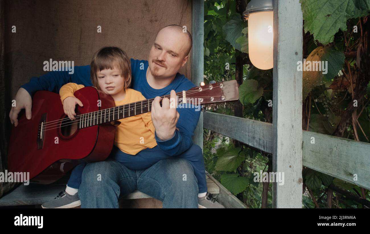 Dad plays an acoustic guitar for his small child. Old, retro decor ...