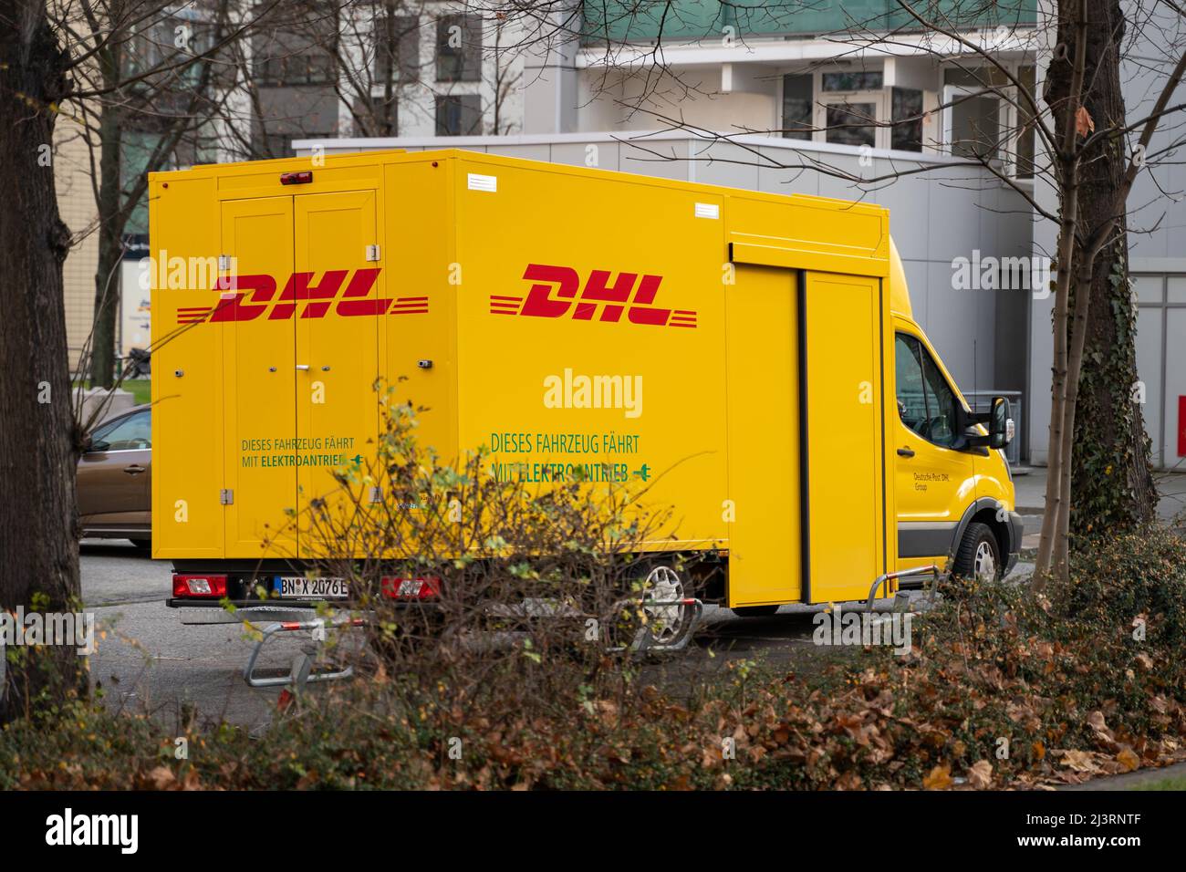 Yellow DHL delivery car parking in front of buildings. Tree and bushes ...