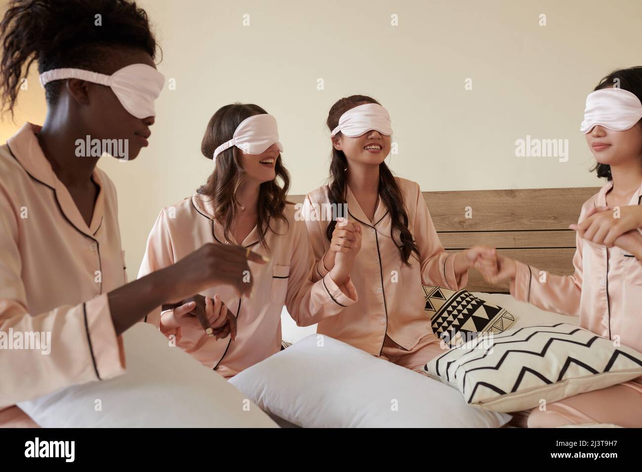 Joyful young women with sleep masks on holding hands and telling ...