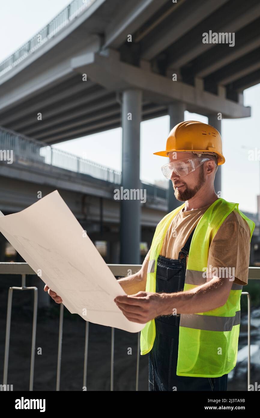 Building worker analyzing project plan and standing on construction ...