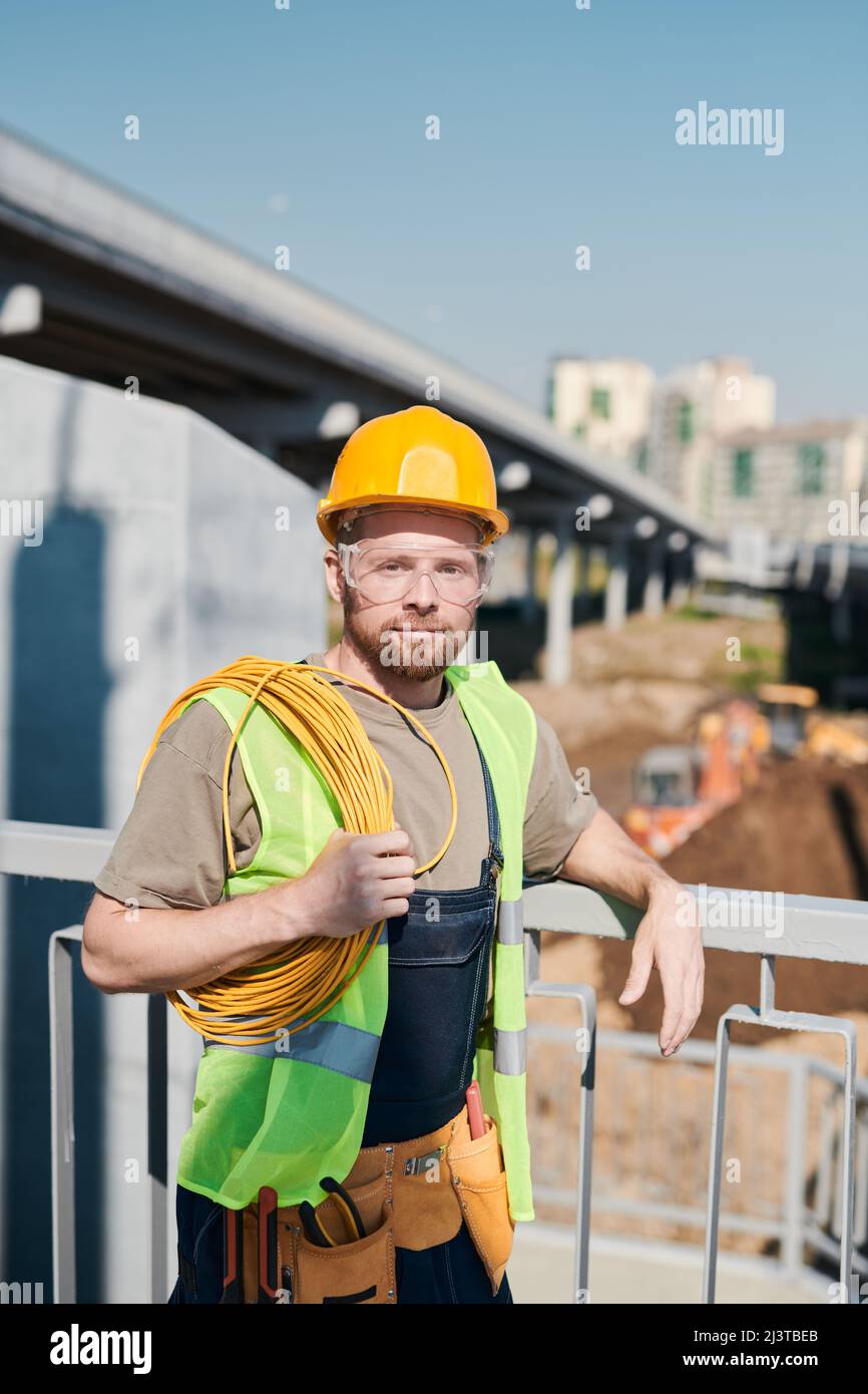 Portrait of young electrician with roll of cable standing at ...