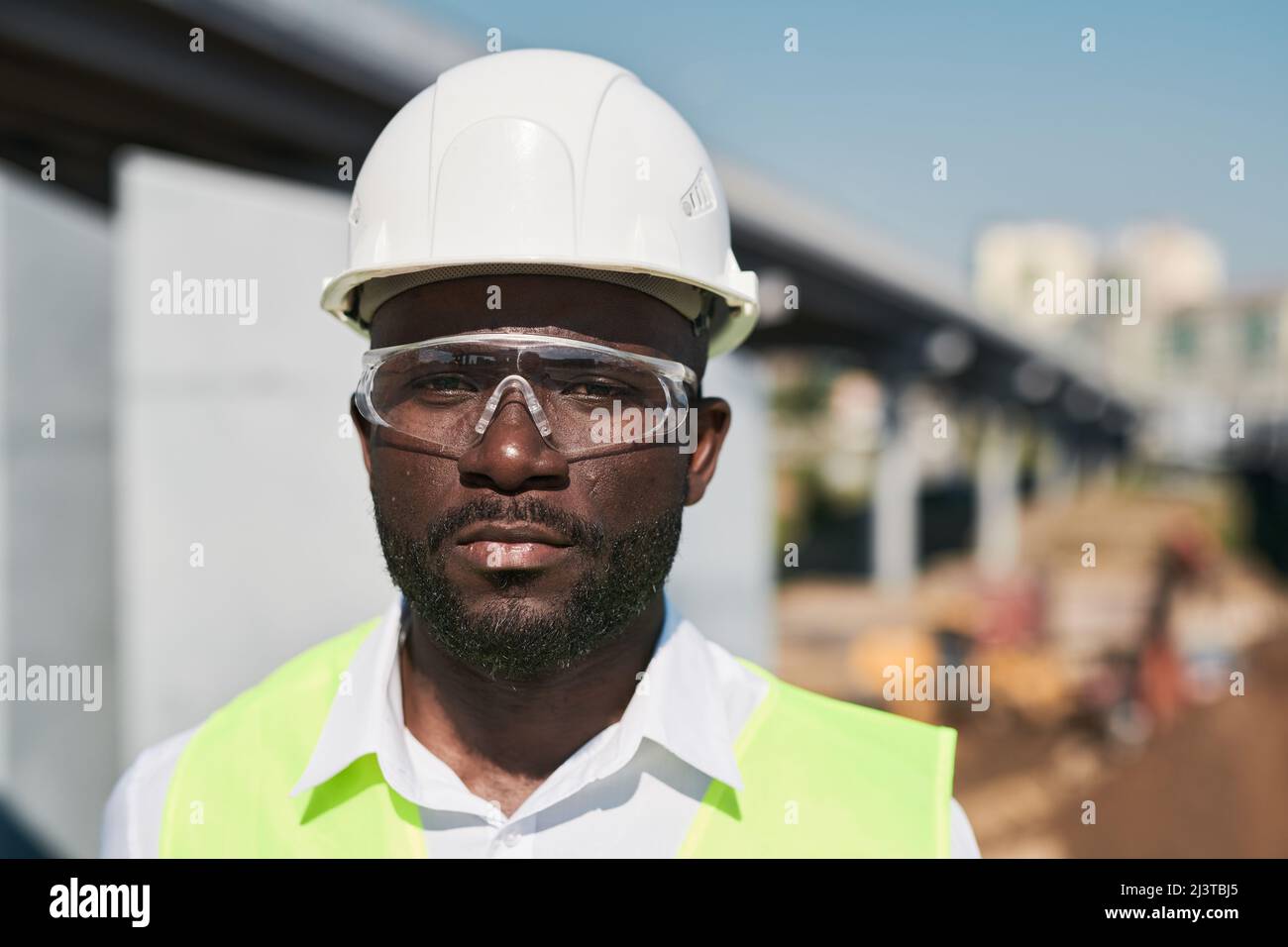 Serious handsome mixed race construction foreman in glasses standing at ...