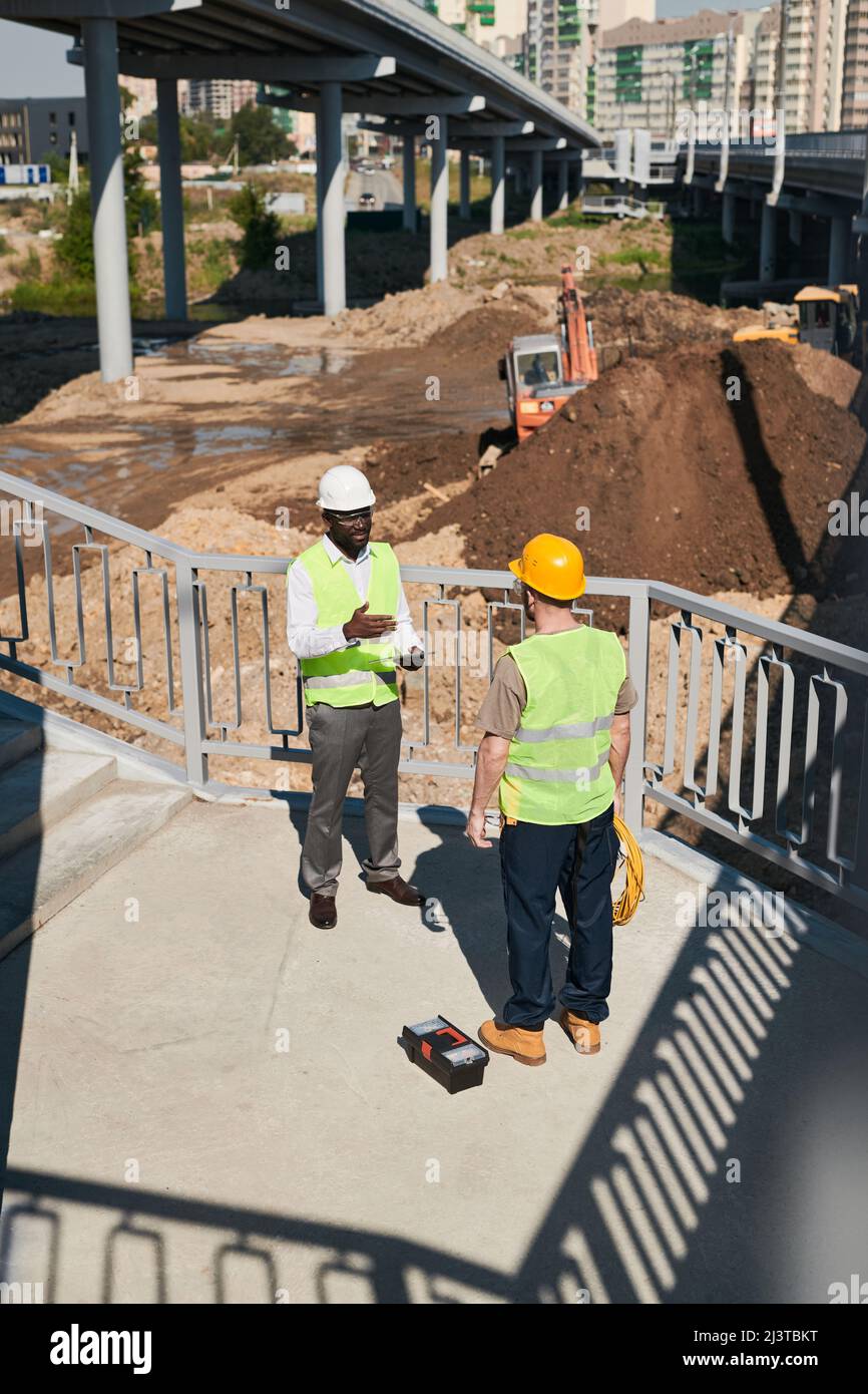 Backlit side view at two construction workers discussing project while ...