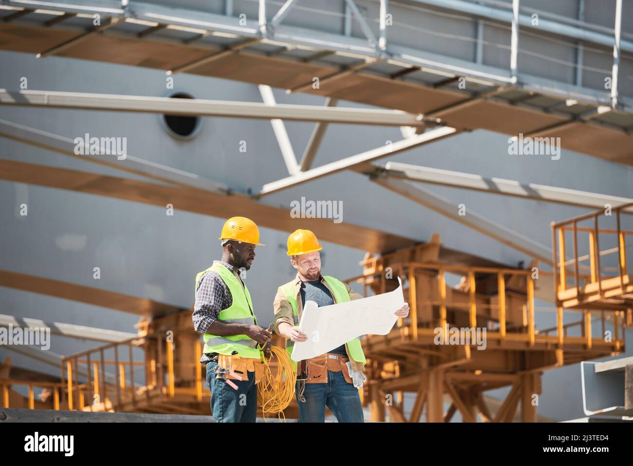 Two construction workers wearing hardhats while chatting at construction site, copy space Stock ...