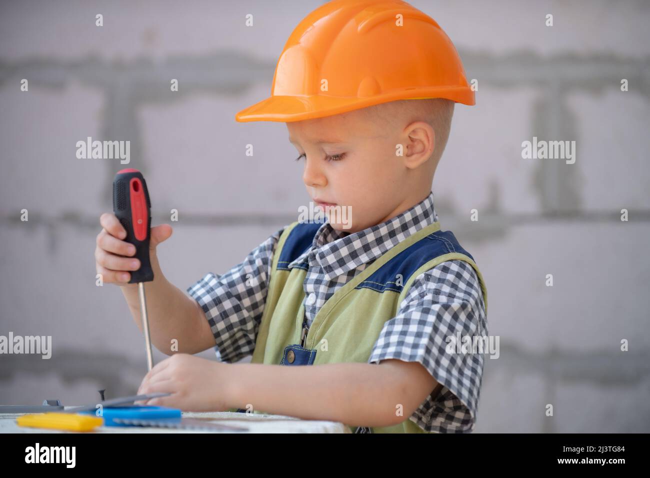 Child play with supplies, tools saw, hammer, screwdriver, helmet ...
