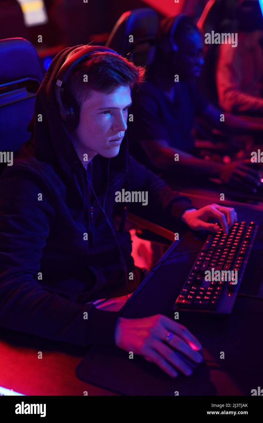 Serious young esports gamer in hoodie wearing headphones playing online ...