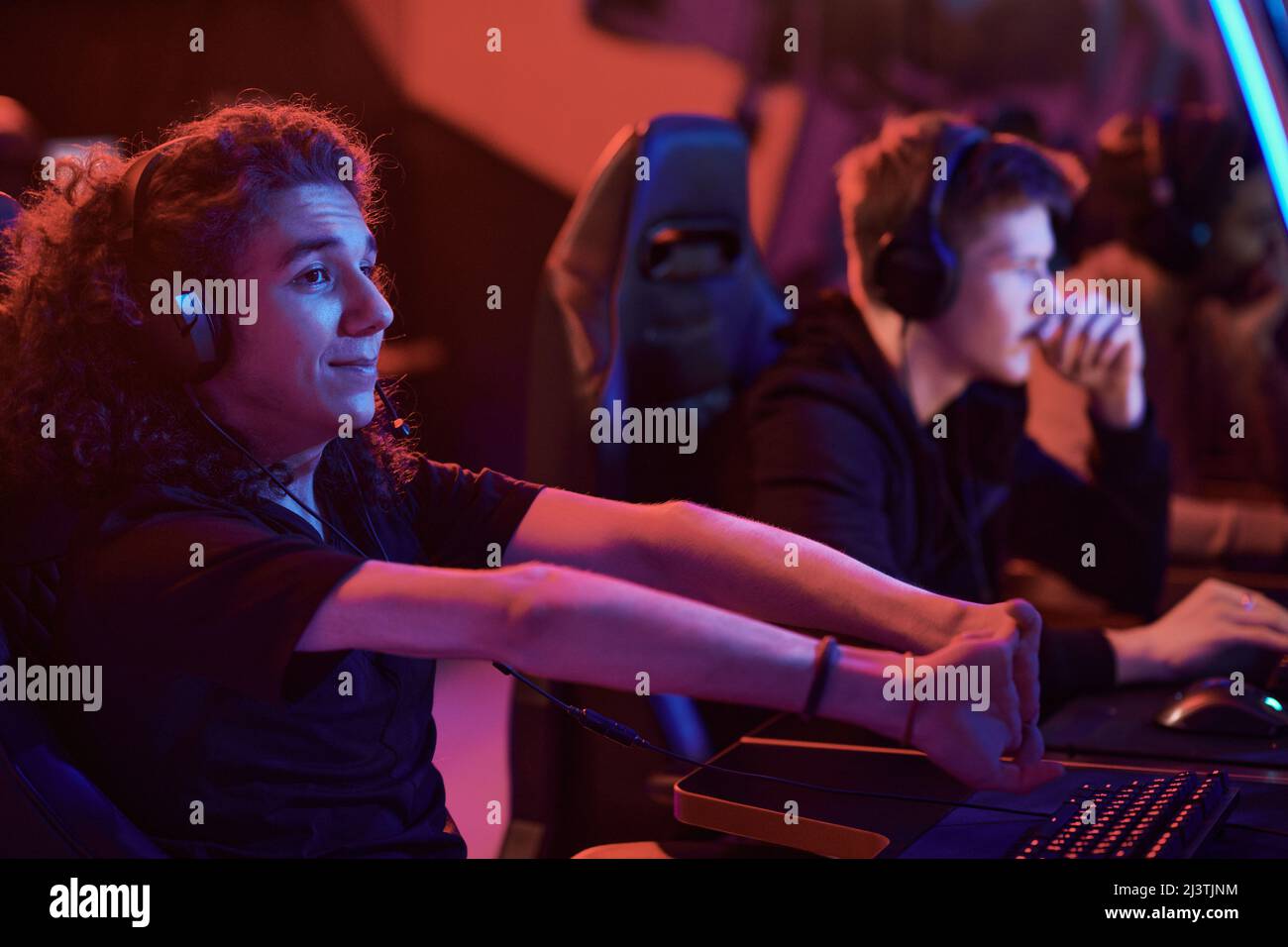 Content young Caucasian computer gamer with long curly hair stretching ...