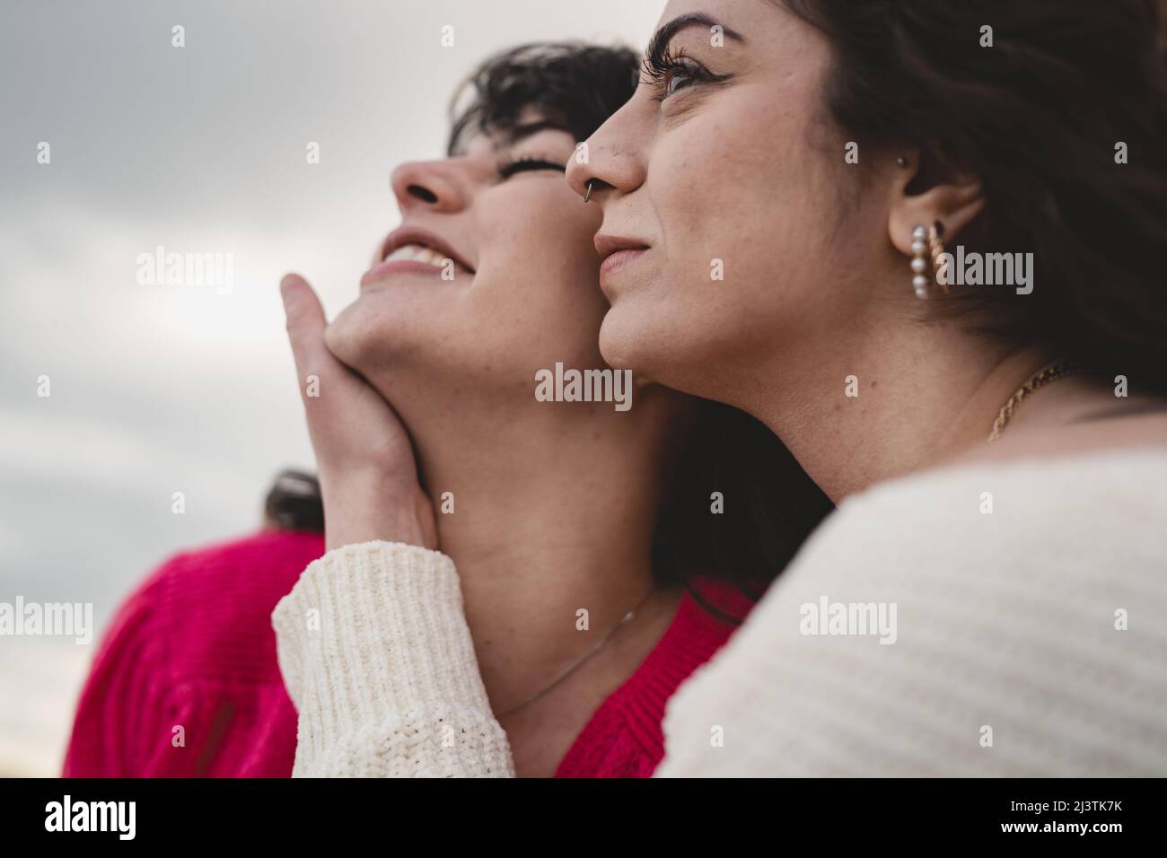 closeup portrait of lovely young girlfriends faces hugging looking outside in a cloudy day ...