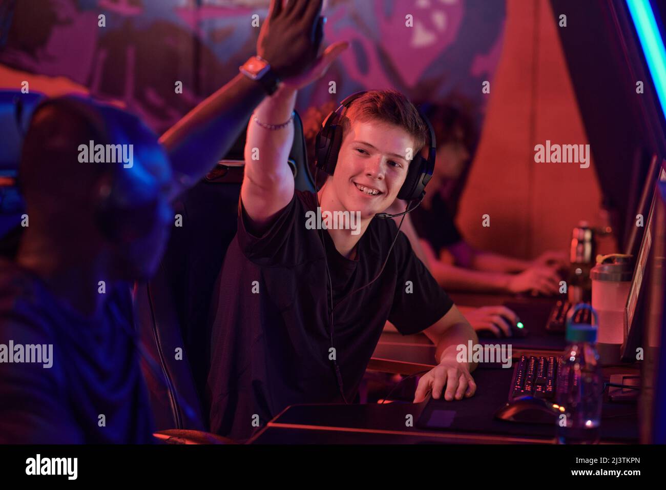 Cheerful team of gamers sitting in dark computer club and giving five ...