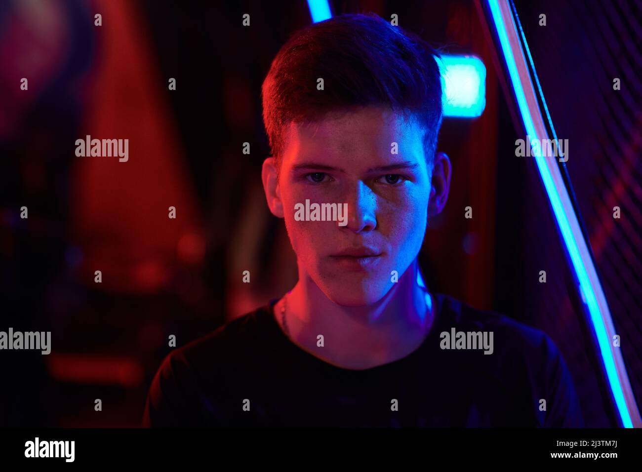 Portrait of serious young Caucasian guy standing in red and blue light ...