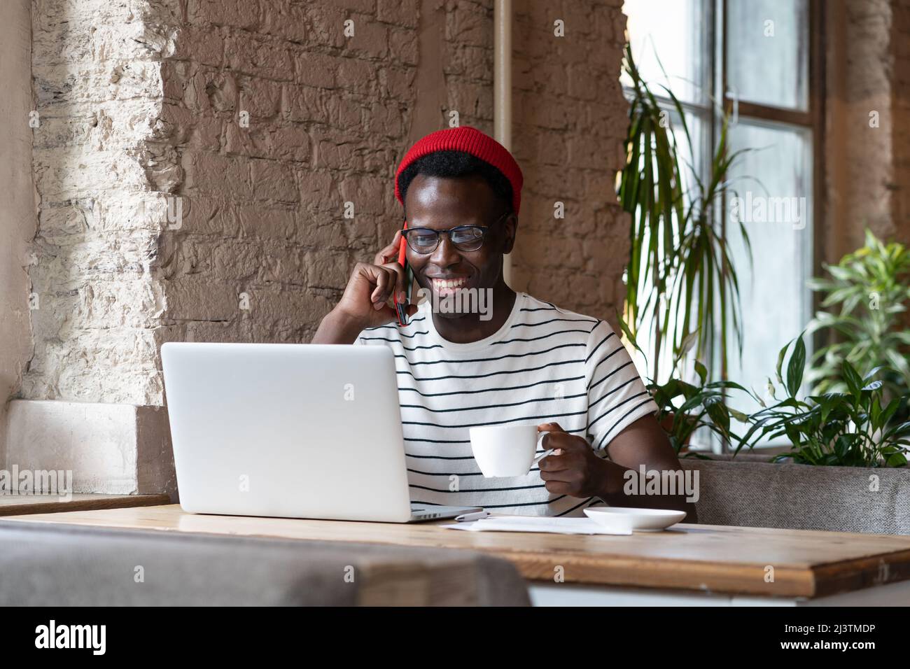 Smiling African man talking on phone, holding cup of coffee, remotely ...