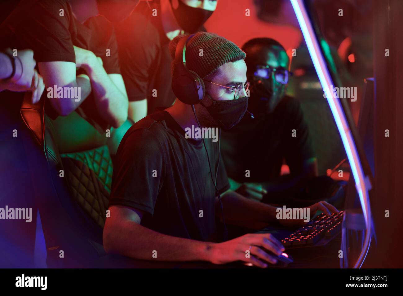 Concentrated young Arabian gamer in hat and cloth mask playing video ...