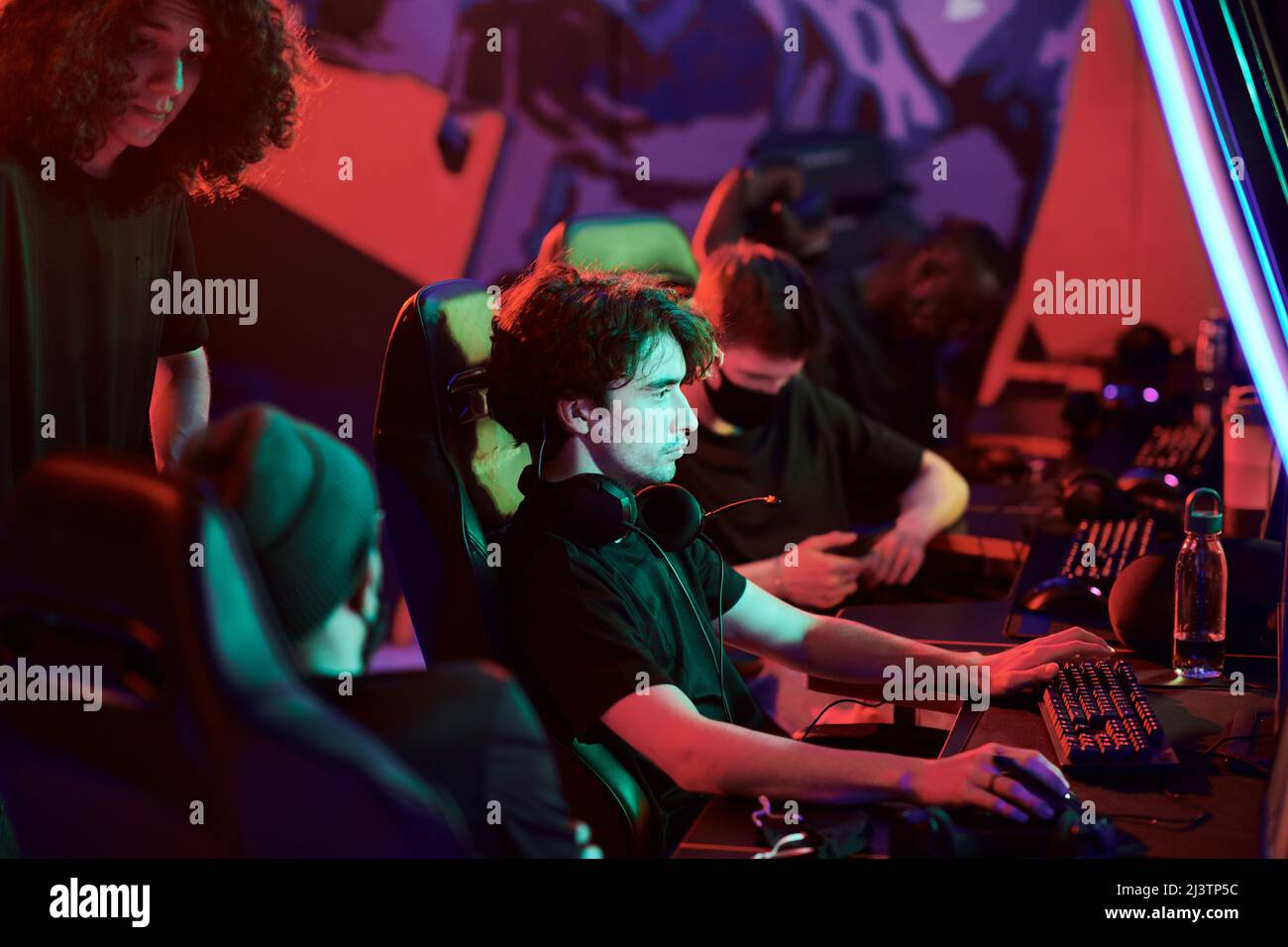 Focused young Caucasian gamer with headphones around neck sitting ...