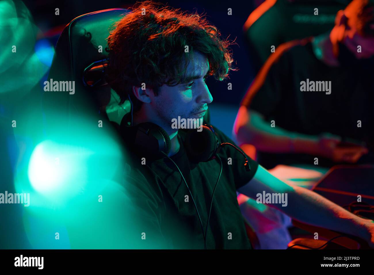 Serious young Caucasian guy with headphones around neck playing online ...