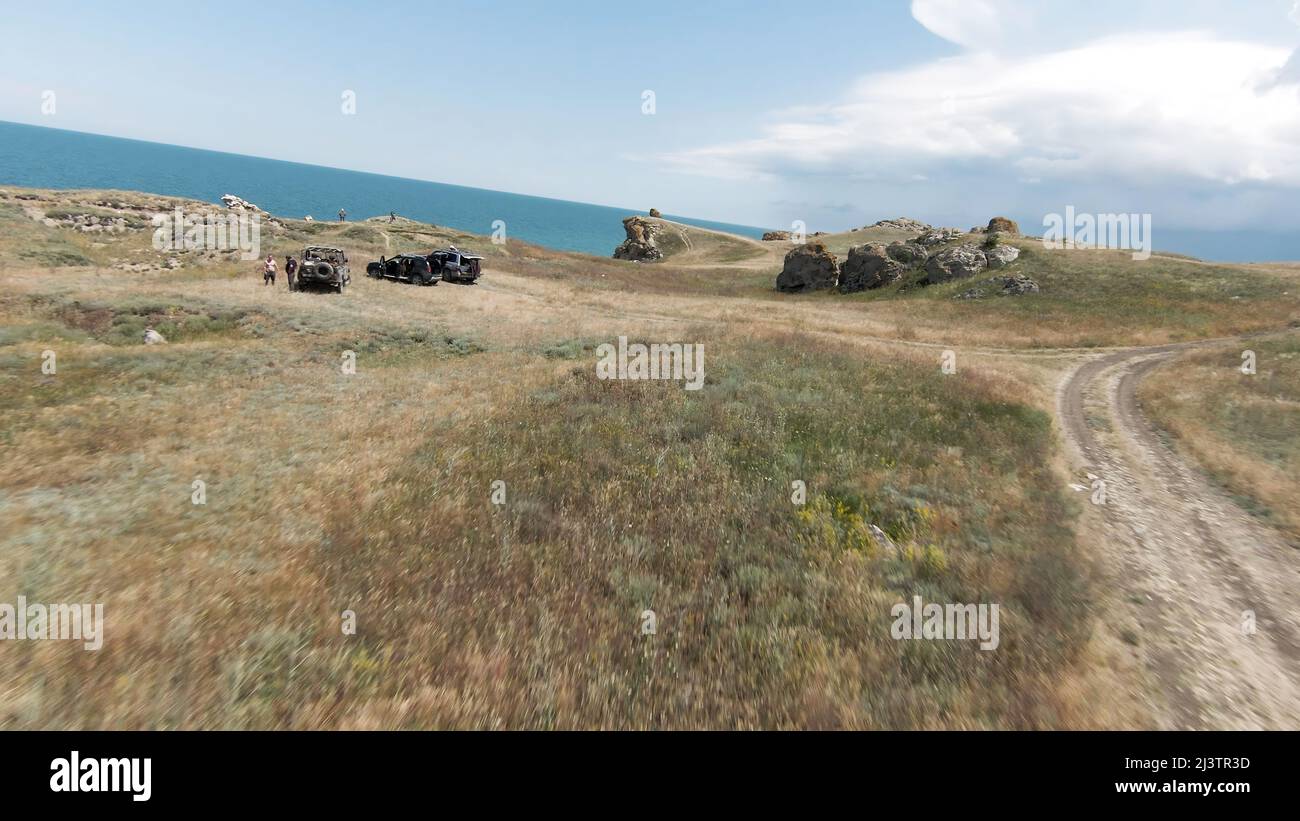 Road on slope on background of sea. Action. Top view of jeeps standing ...