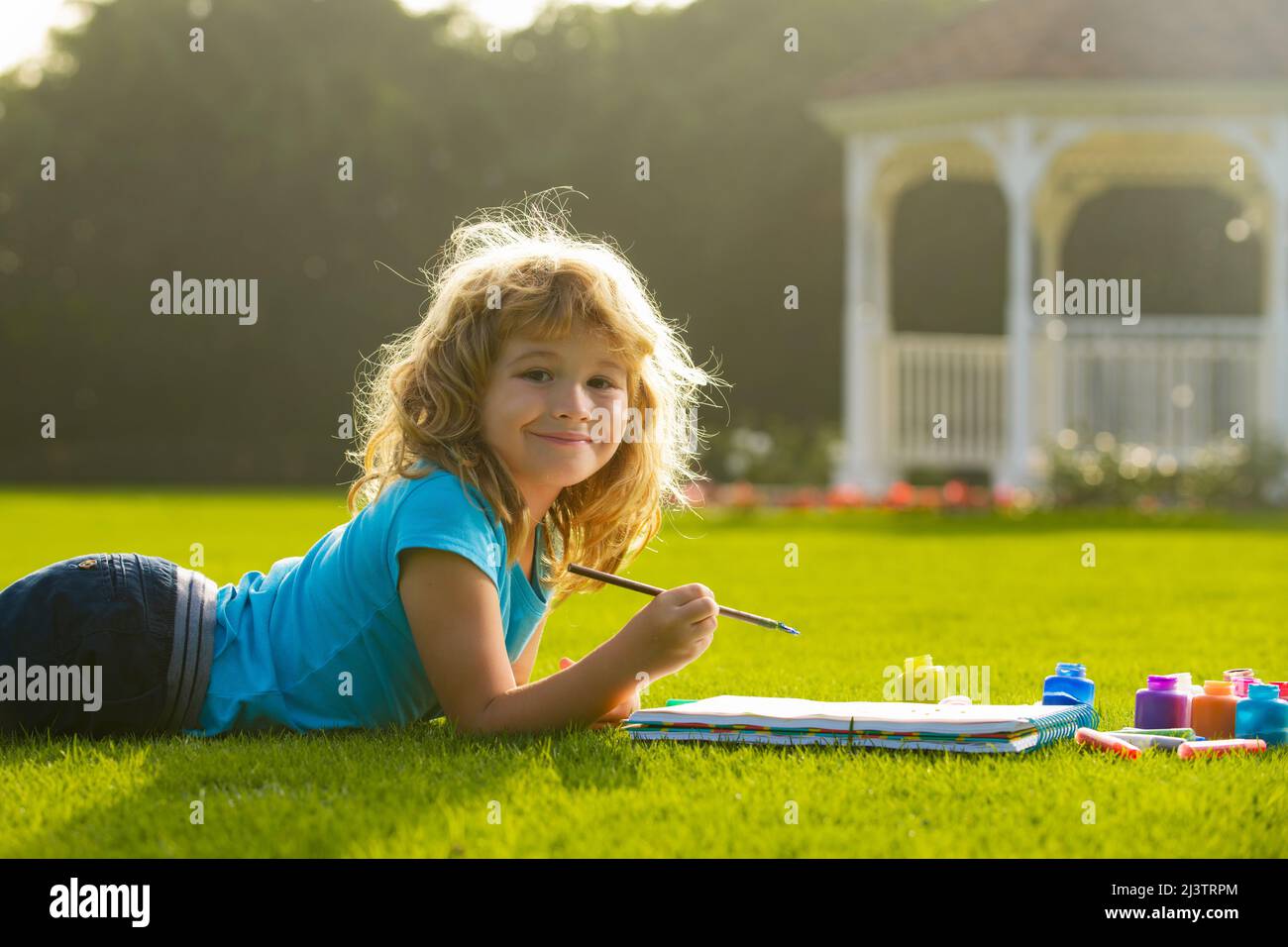 Kid draws in park laying in grass having fun on nature background ...